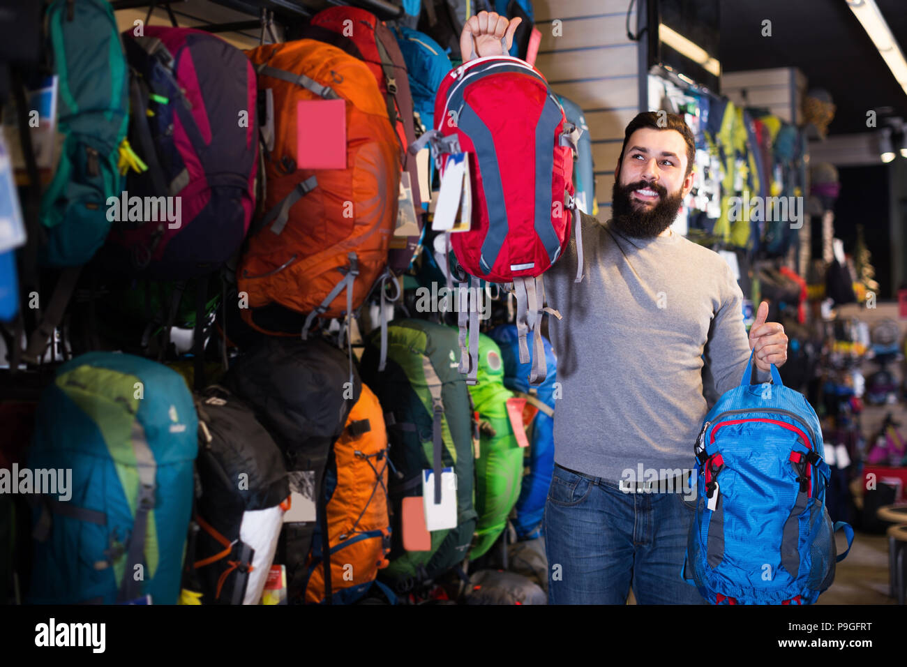 Young man customer examining backpacks in sports equipment store Stock ...