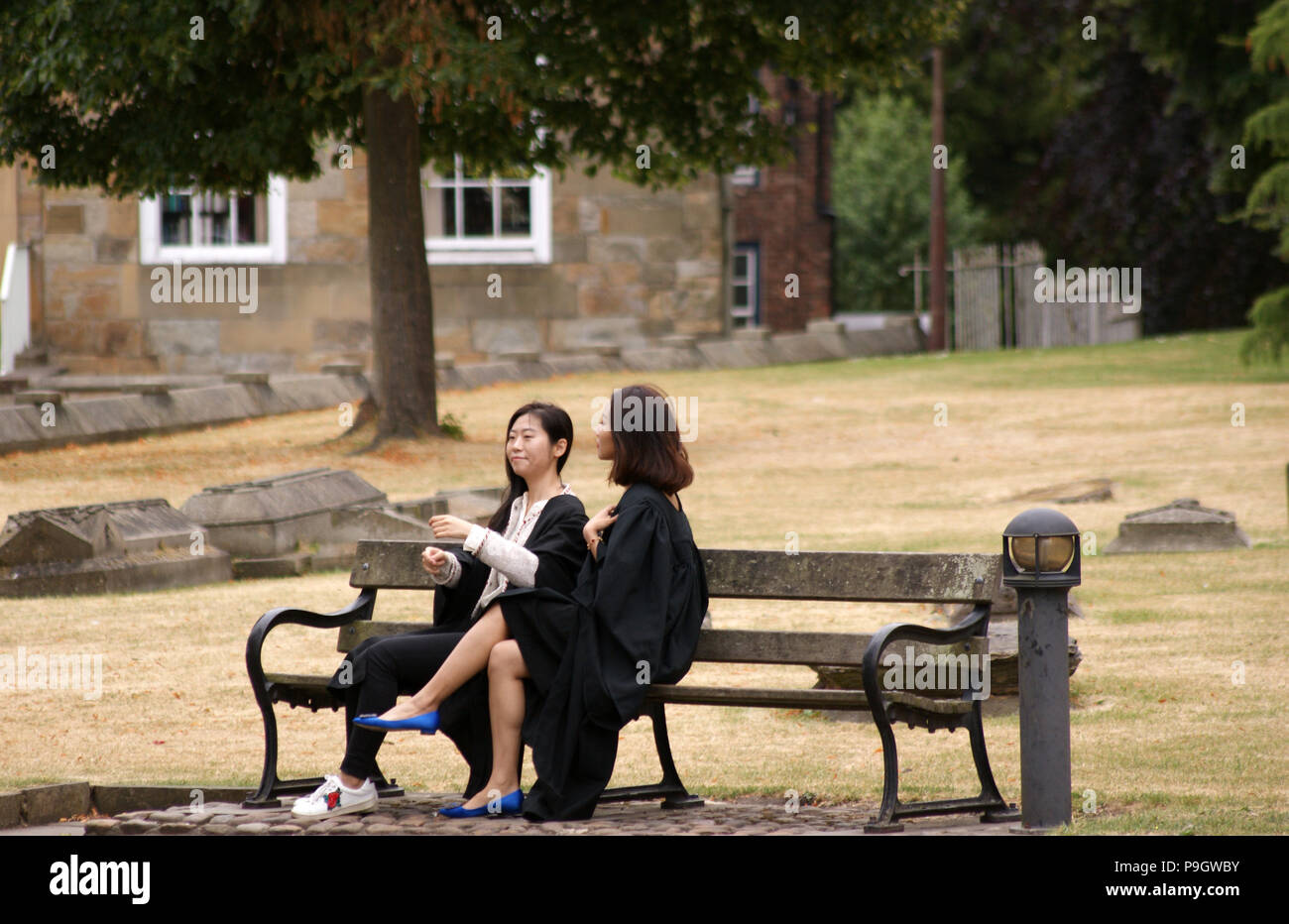 Two Durham University Graduates seated on a bench one is wearing a gown ...