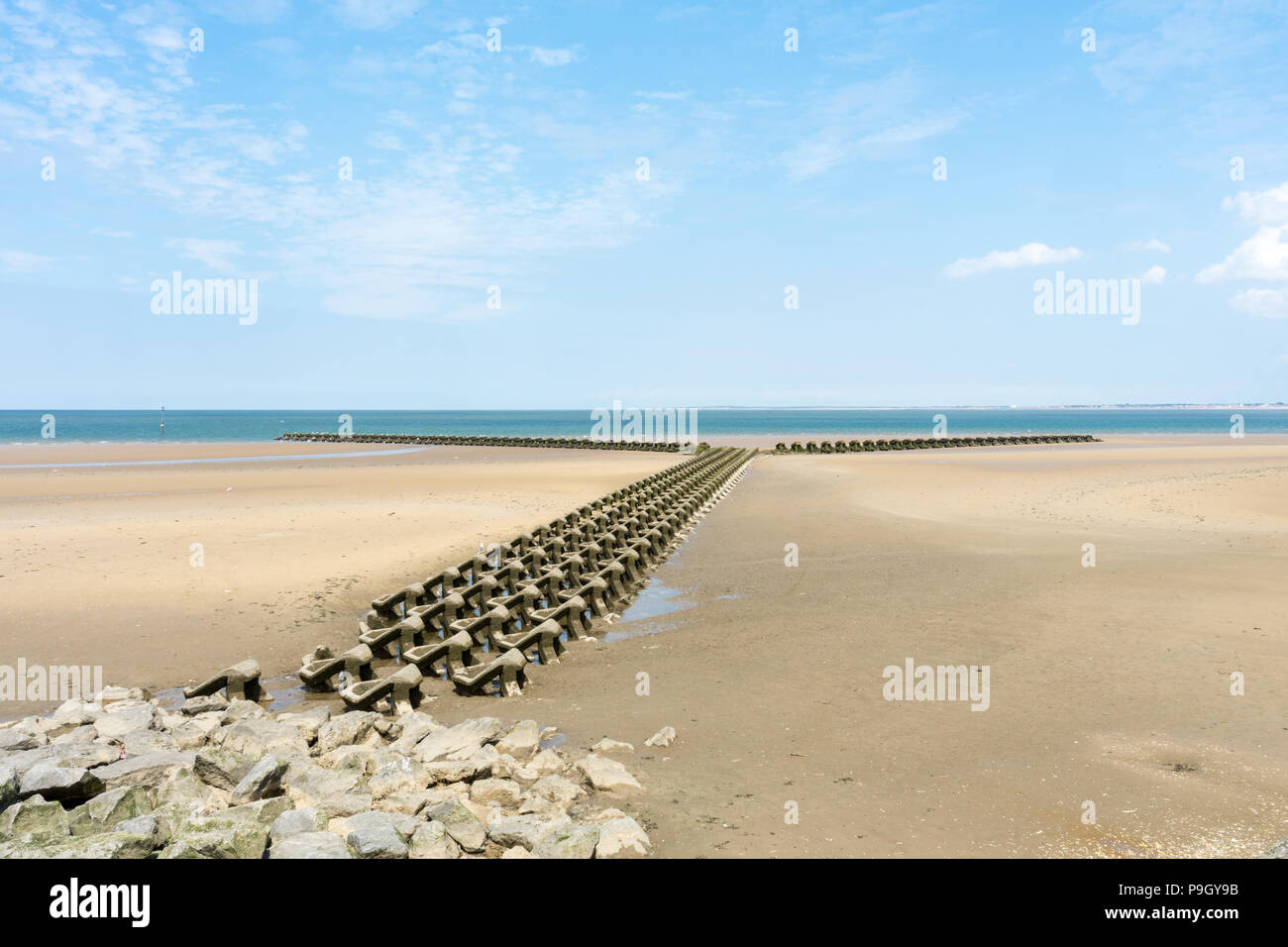 Beach scene with sand, blue sea, blue sky, rocks and wave defence Stock ...