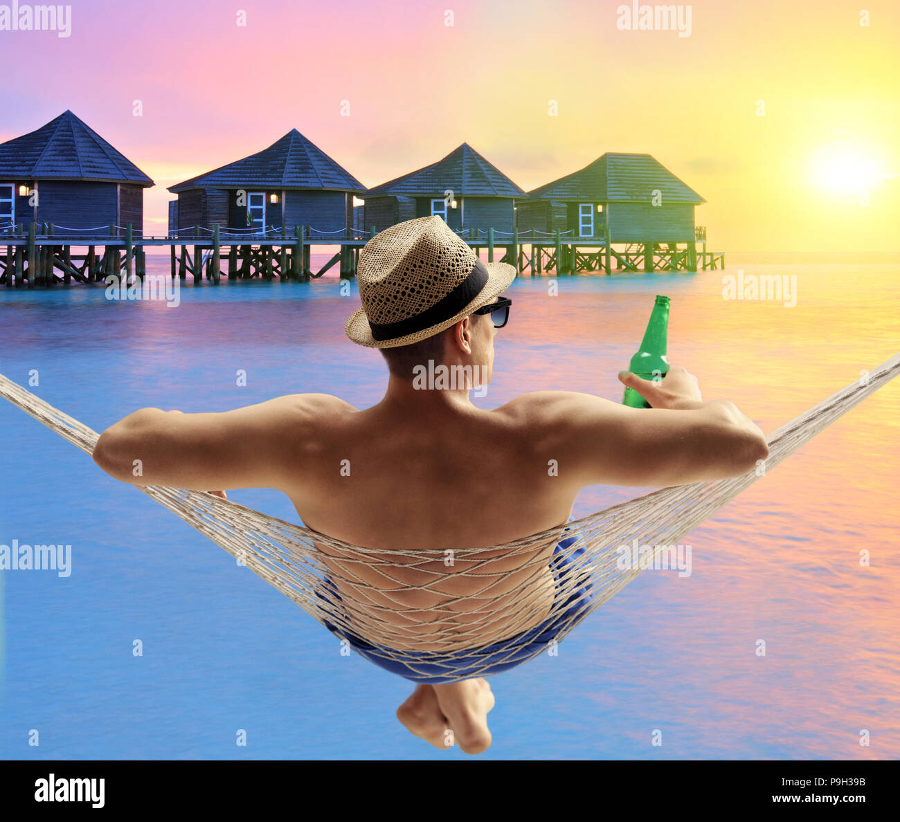 Young man with a bottle of beer lying in a hammock at a water cottages ...