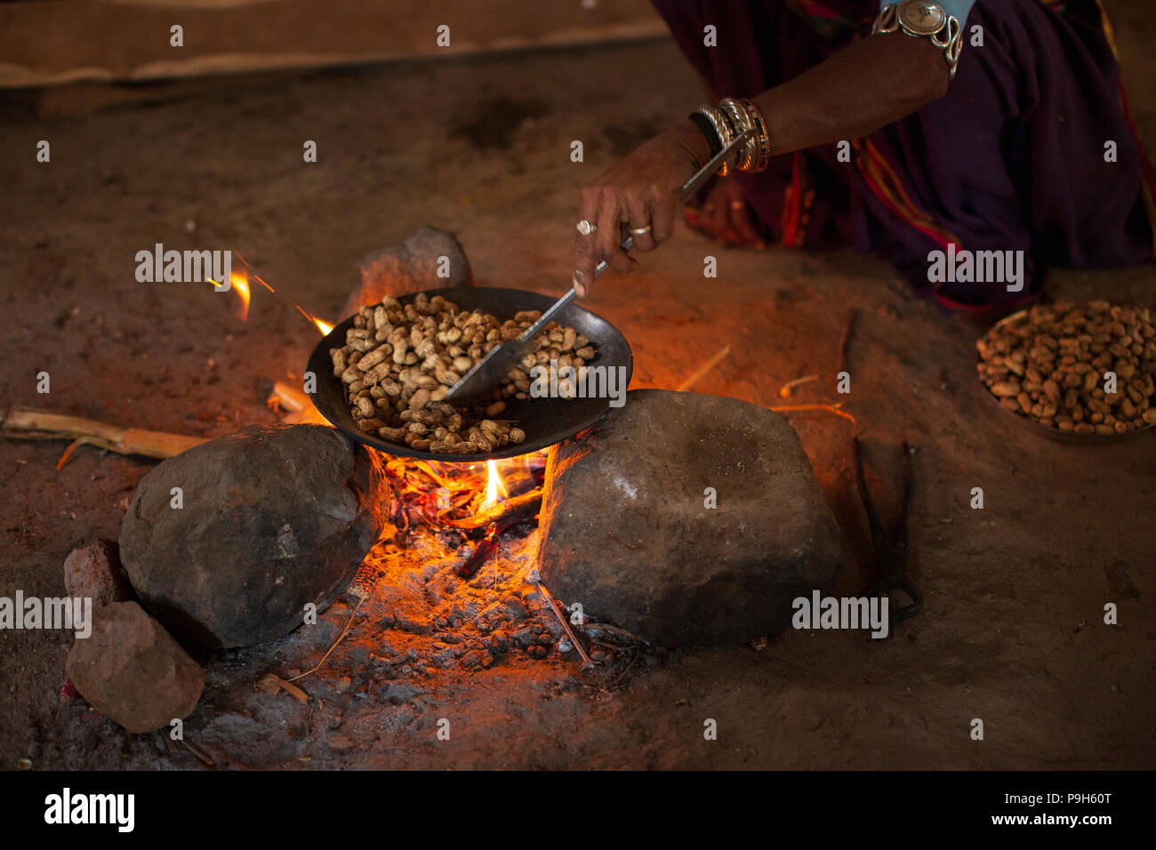 A woman roasting groundnuts on an open fire at their home in rural ...