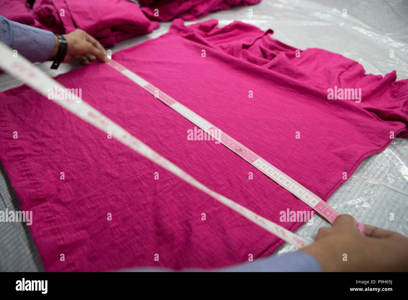 A man measuring a T-shirt on a production line in a garment factory ...