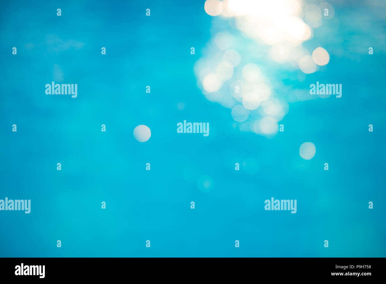 Soft focus bokeh light effects over a rippled, blue water background in ...