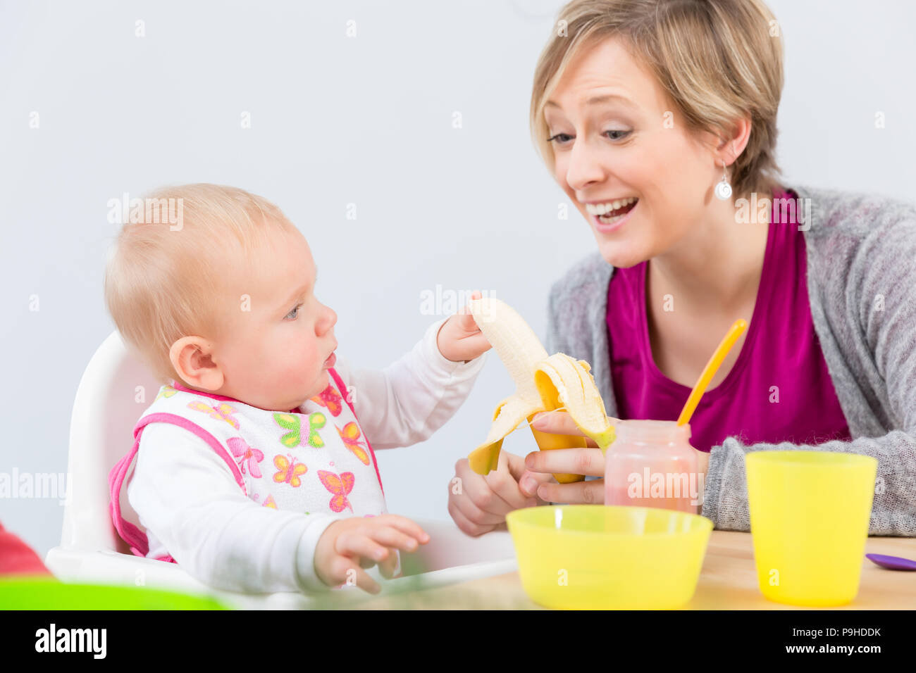 happy mother giving a fresh and nutritious banana to her cute baby girl ...