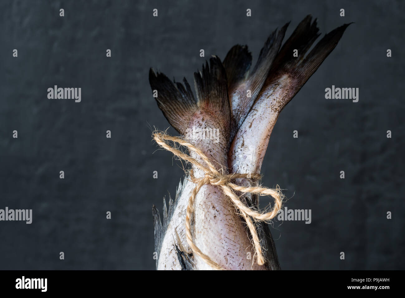 Raw fish tails tied with rope with bow on dark background. Selective ...
