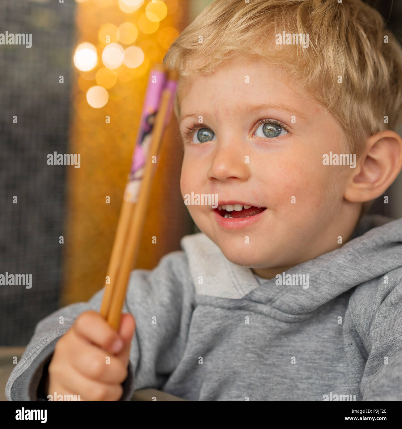 Baby boy sitting in high chair plays with chopsticks and smiling ...