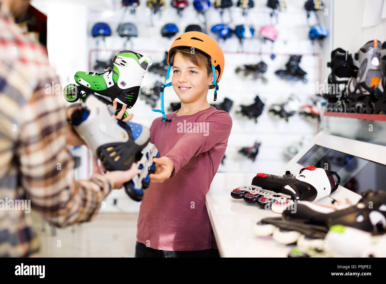 happy male shop assistant helping smiling european boy to choose roller ...