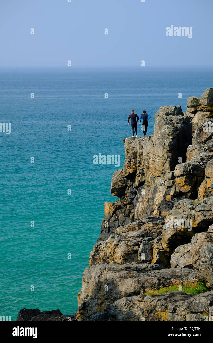 Two young men stand at a cliff top on the Cornish coast about to jump ...