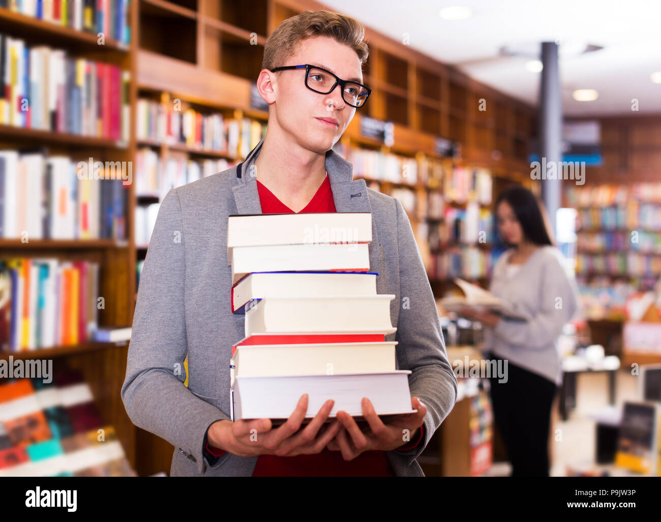 Portrait of weary guy with stack of books in hands in bookstore Stock ...
