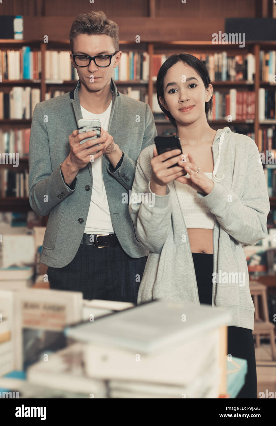 Young students using phones while studying together in library Stock ...