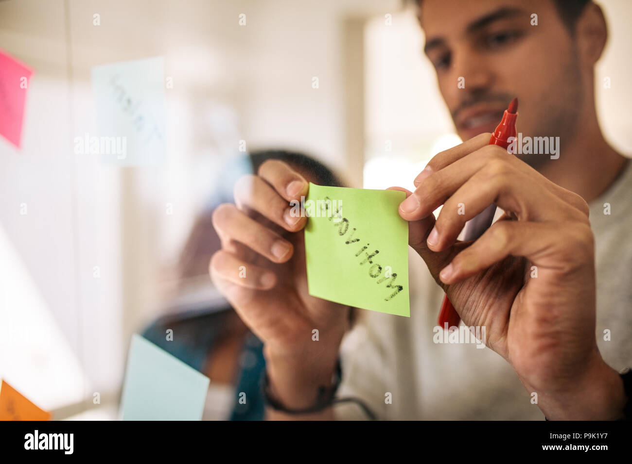 Man writing on sticky notes with marker pen and pasting on glass board ...