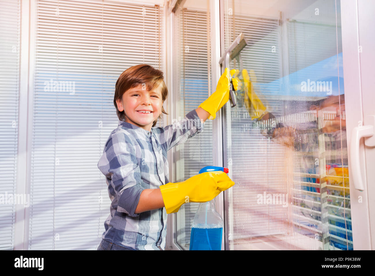 Portrait of seven years old boy in yellow rubber gloves washing windows ...