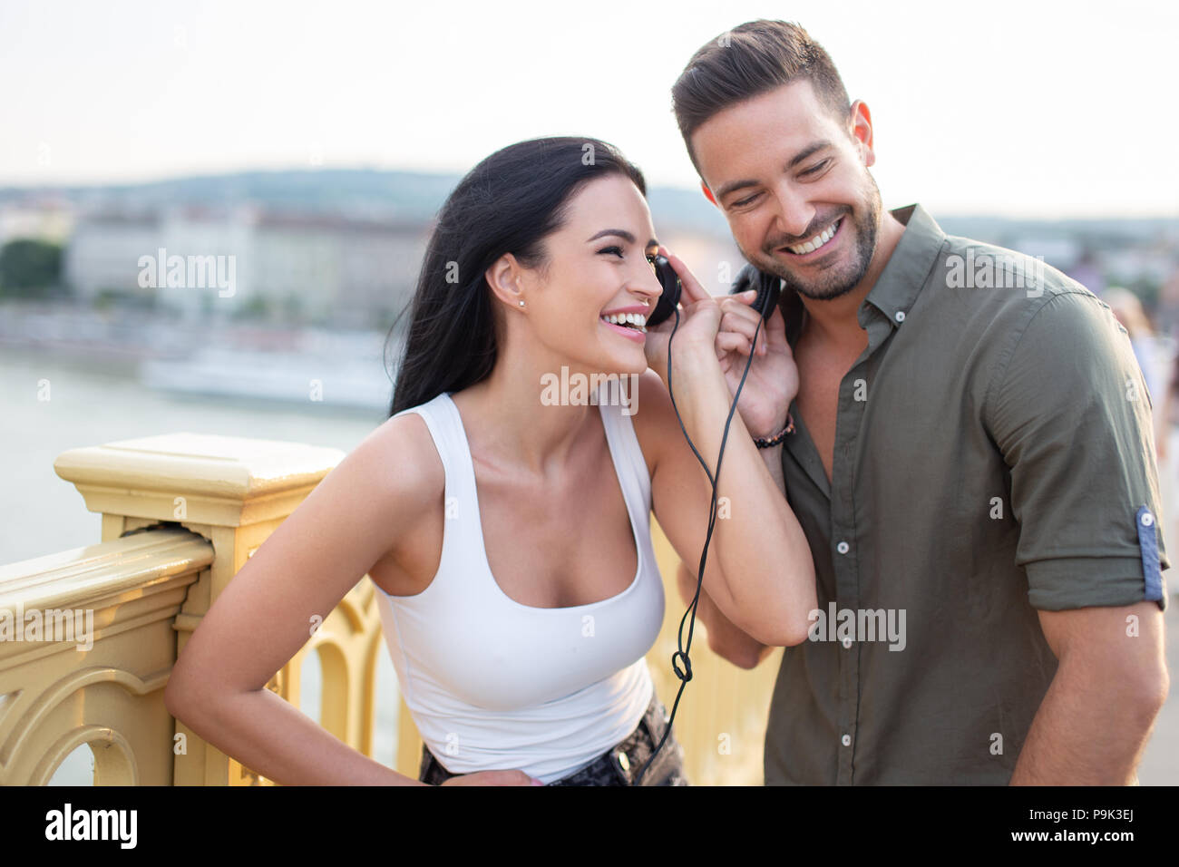 Happy young couple listening music outdoors, sharing headphones Stock ...