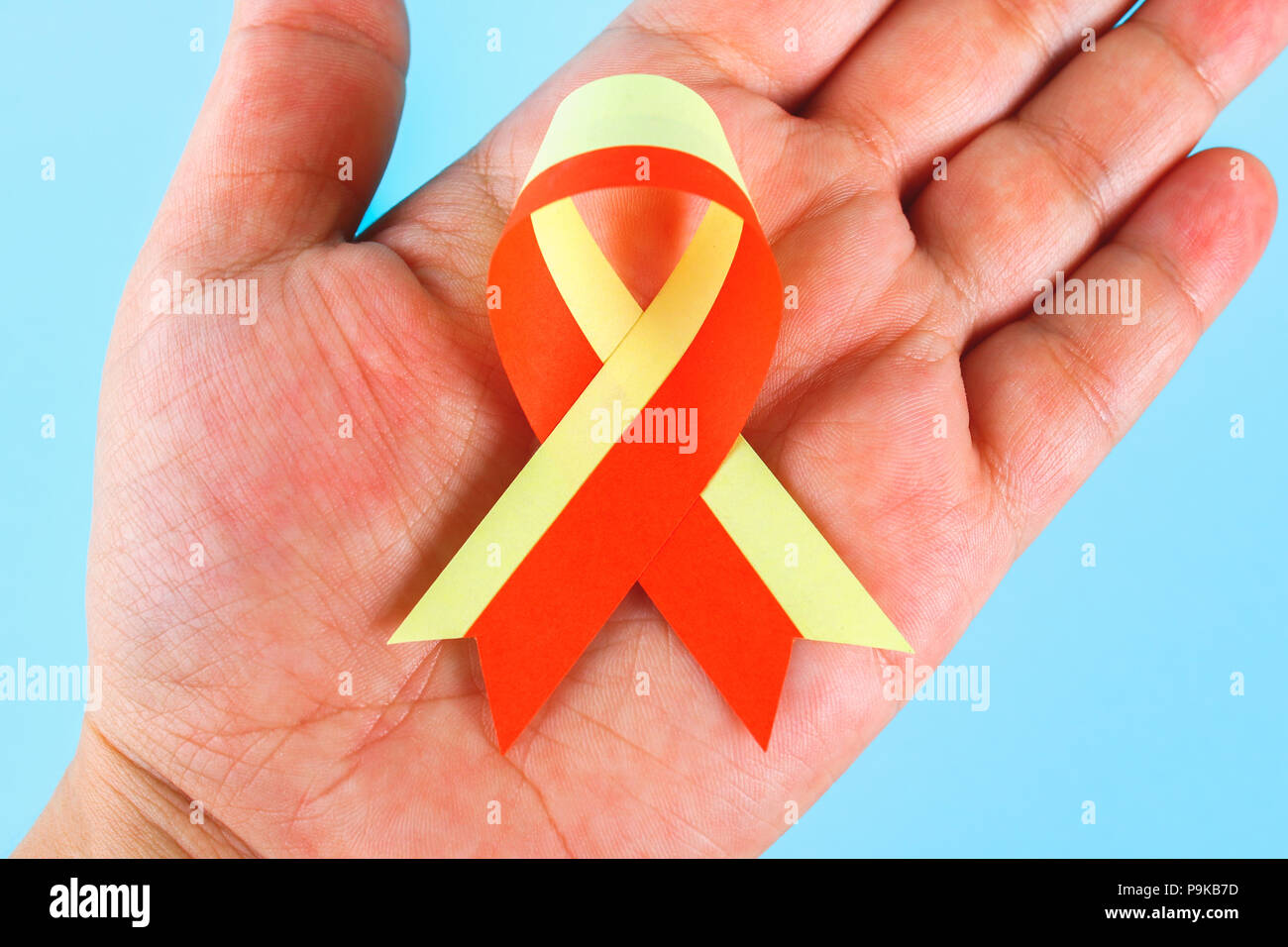 World Hepatitis Day. June 28th. Red yellow ribbon on hand on a blue ...