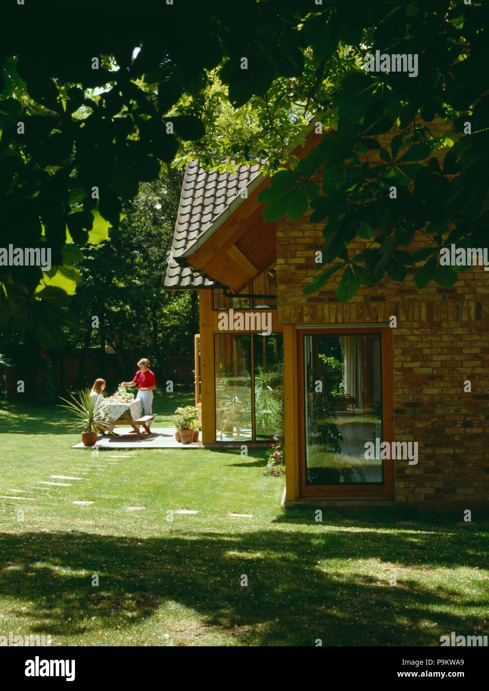 People on patio outside modern house in the country with large lawn FOR ...