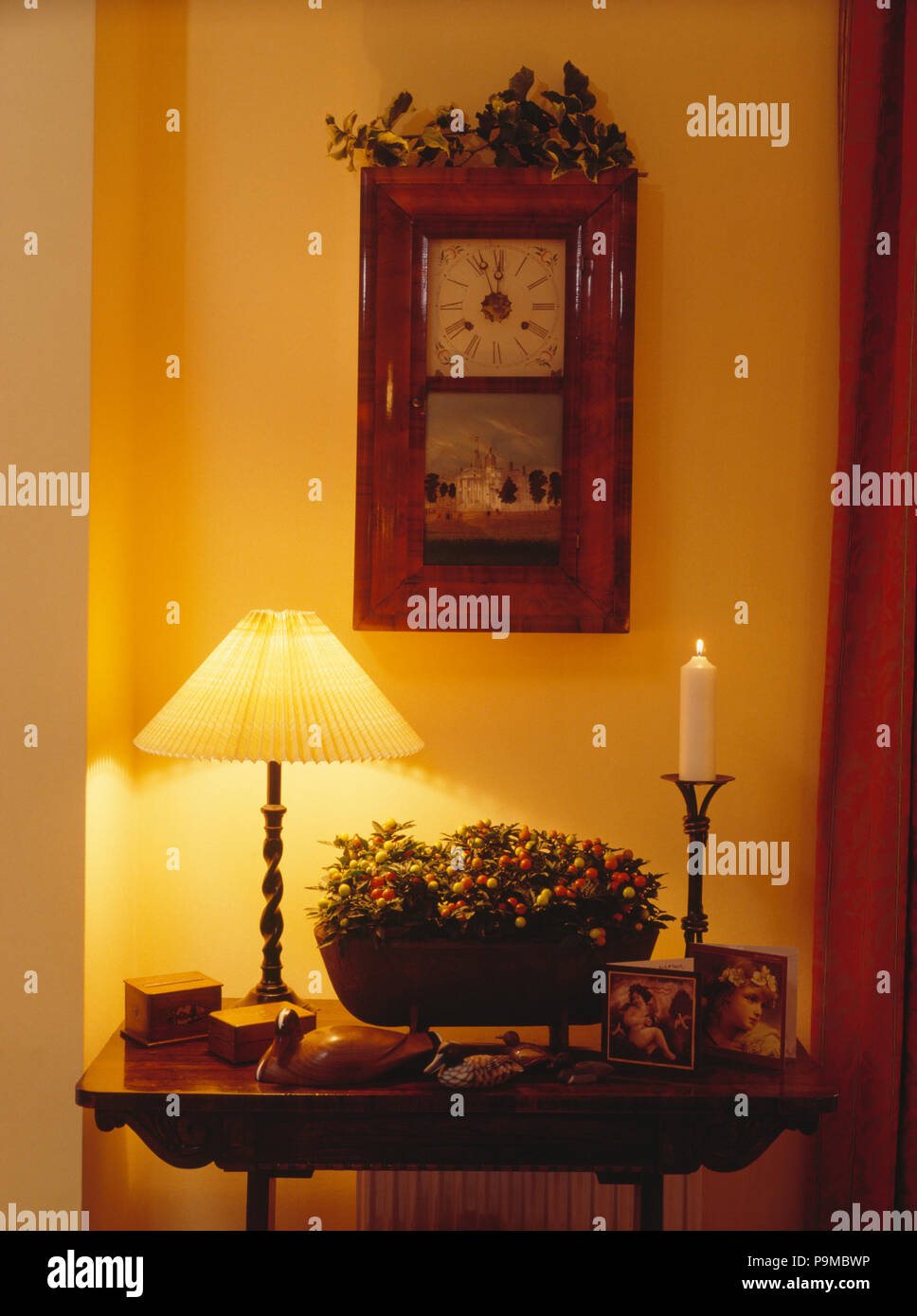 Antique clock with painted scene above lighted lamp on small table in ...