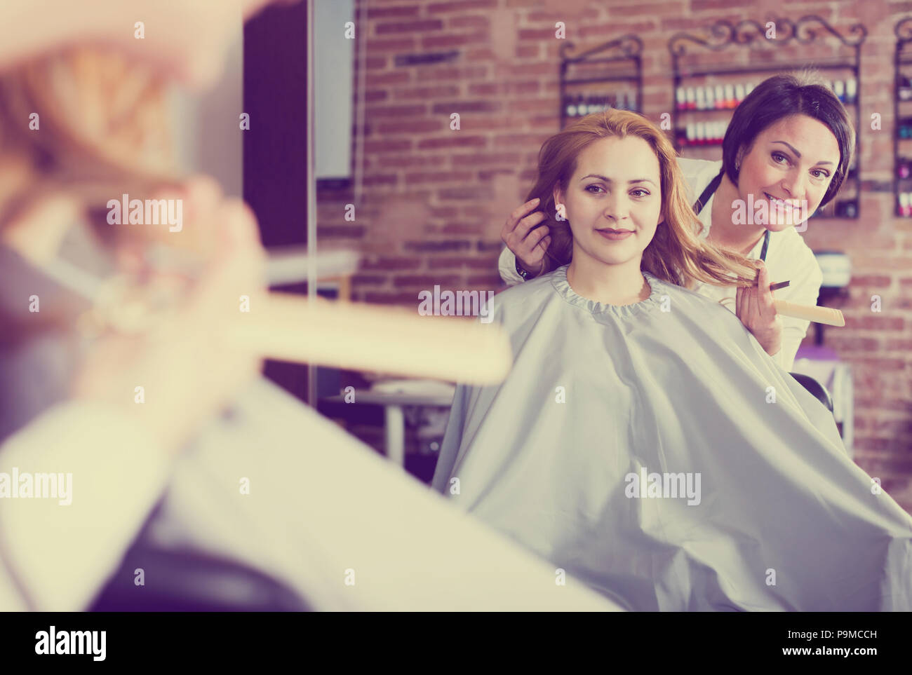 Happy young woman consults with master in hairdress salon about hair ...