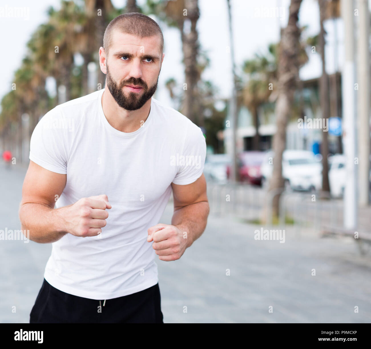 Athletic male in a white t-shirt running along the sidewalk in the city ...