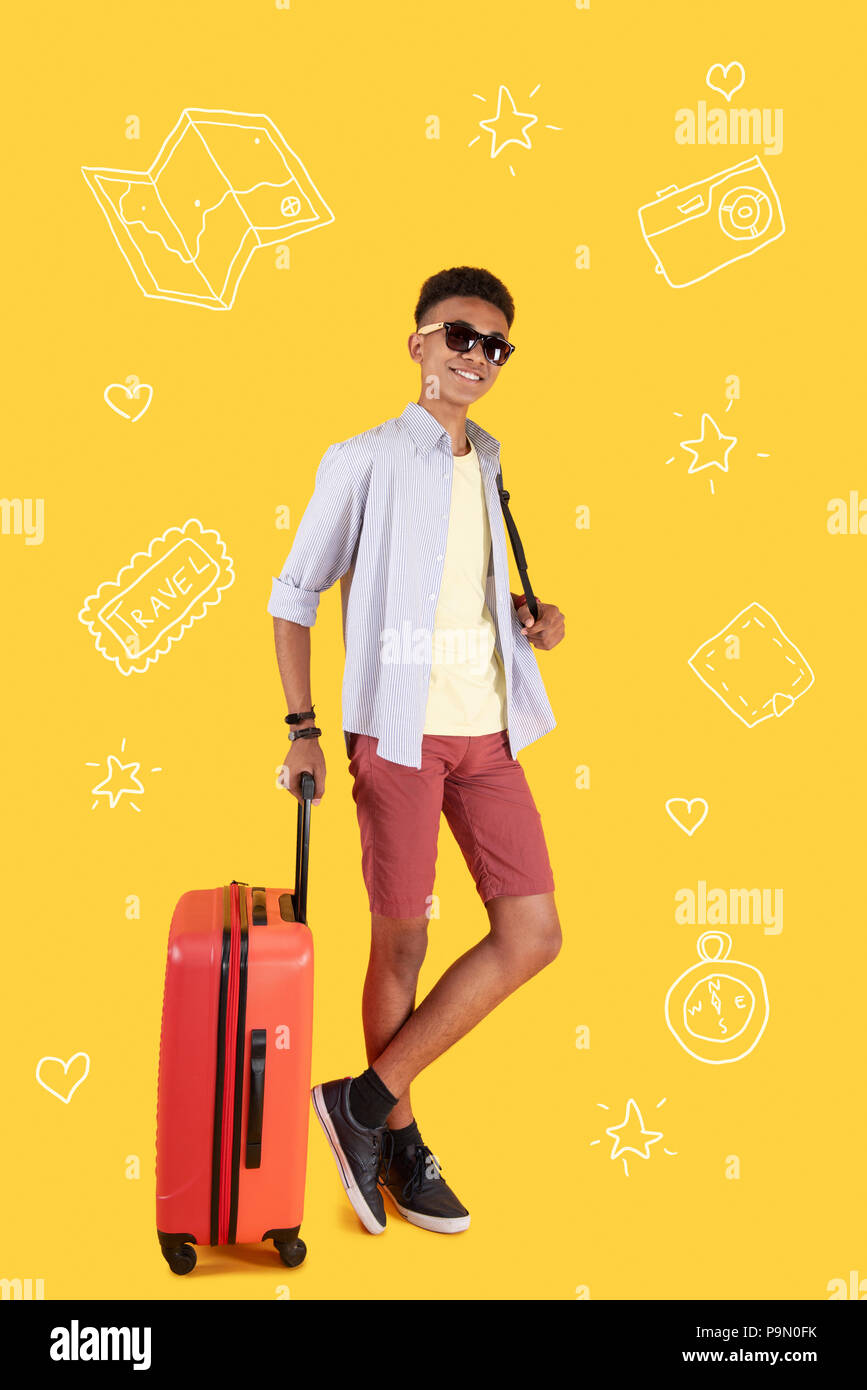 Positive student smiling and carrying his luggage while travelling ...