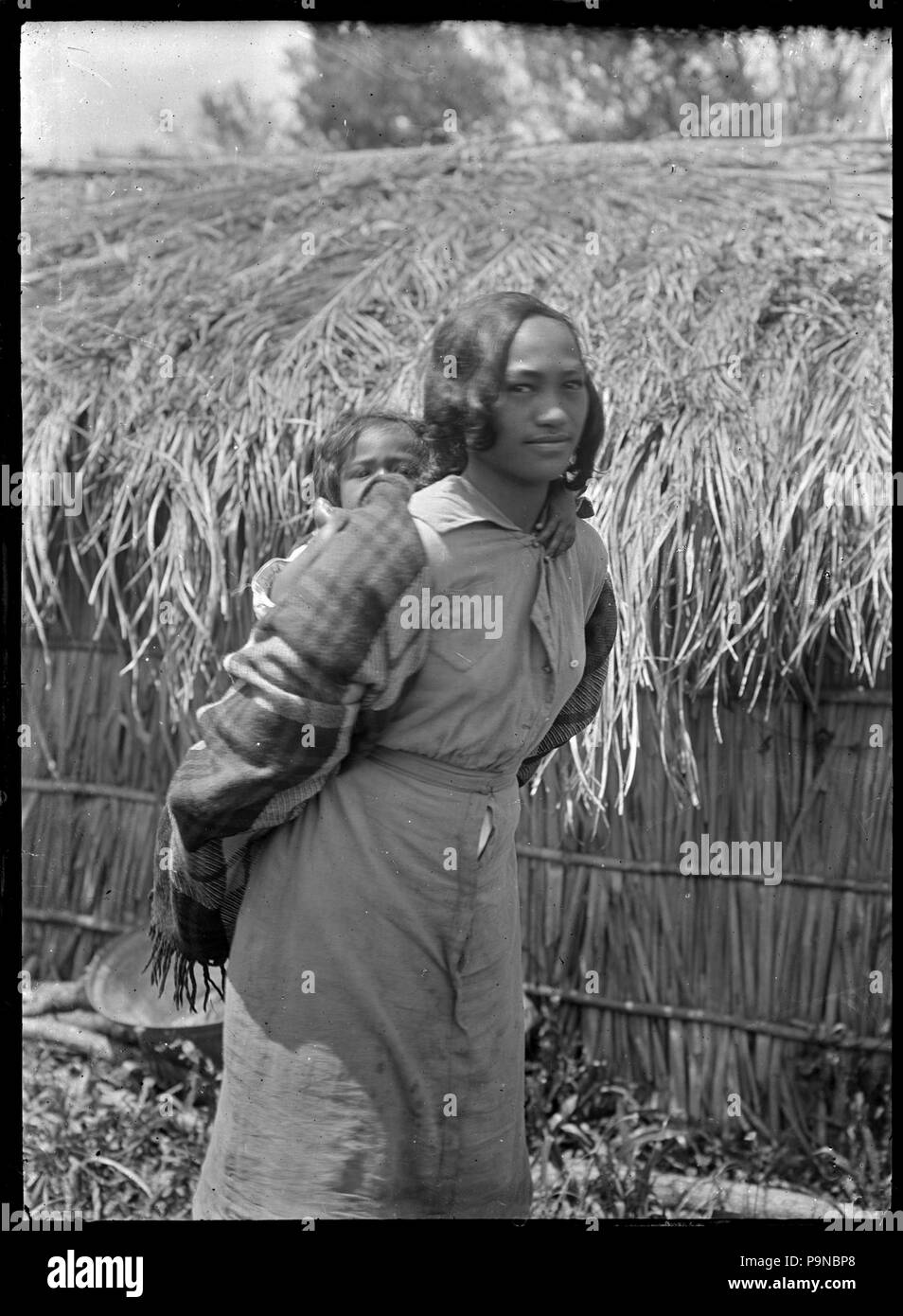 334 Young Maori woman carrying a child on her back, standing outside a ...