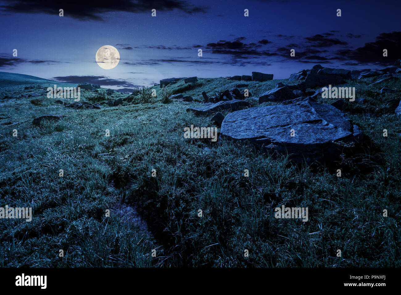cloud over the grassy hillside with rocks at night in full moon light ...