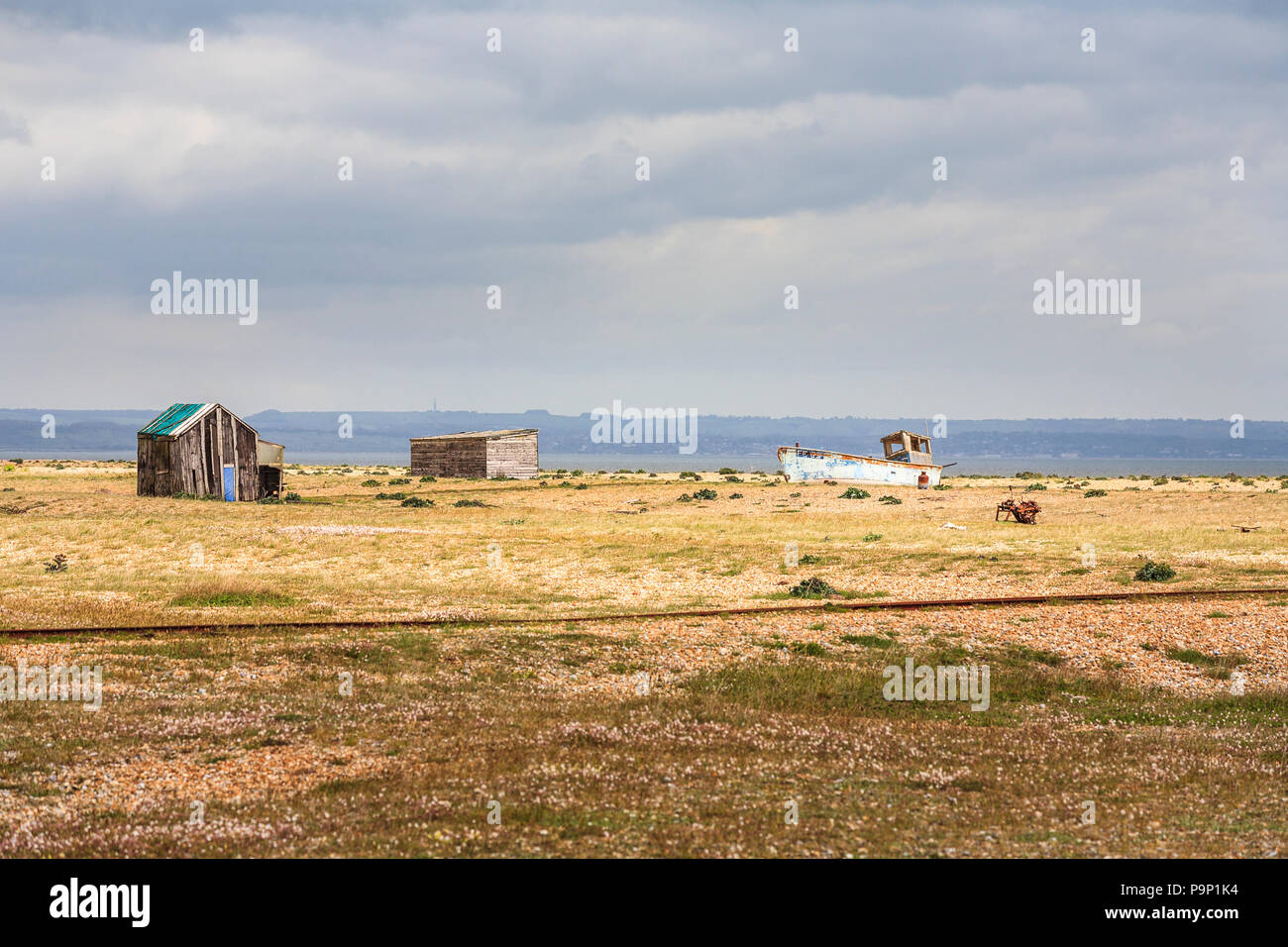 Old wooden huts and an abandoned fishing boat on the shingle beach at ...