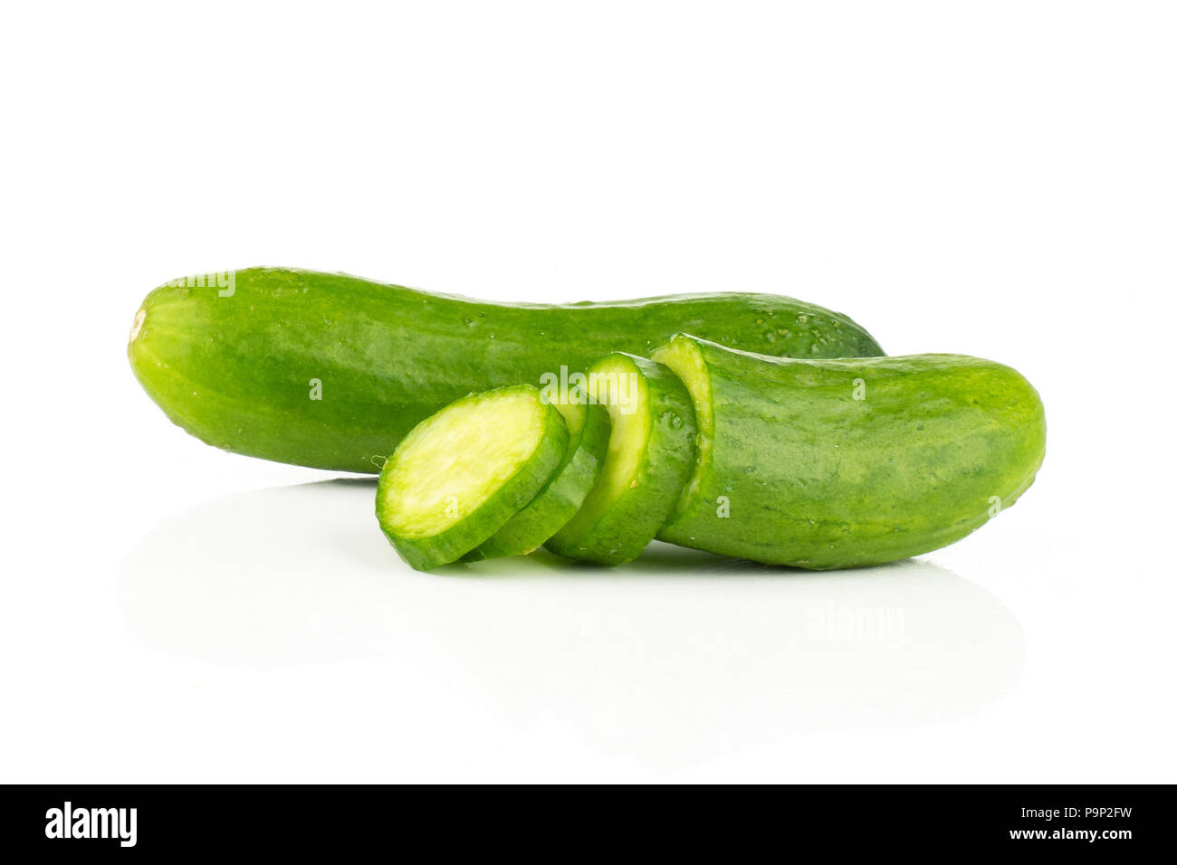 One fresh green mini cucumber with a sliced half and three slices ...