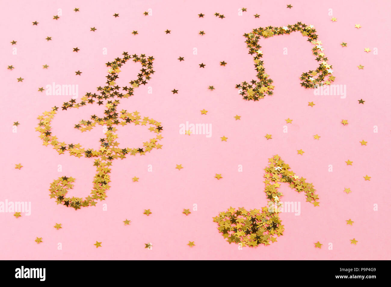 Musical notes of starry golden confetti lying on a pink pastel ...
