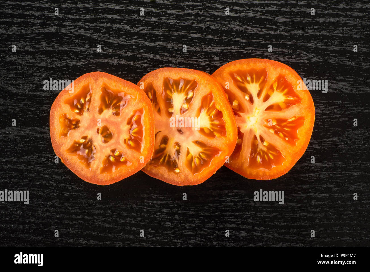 Three red tomato slices top view isolated on black wood background cut ...