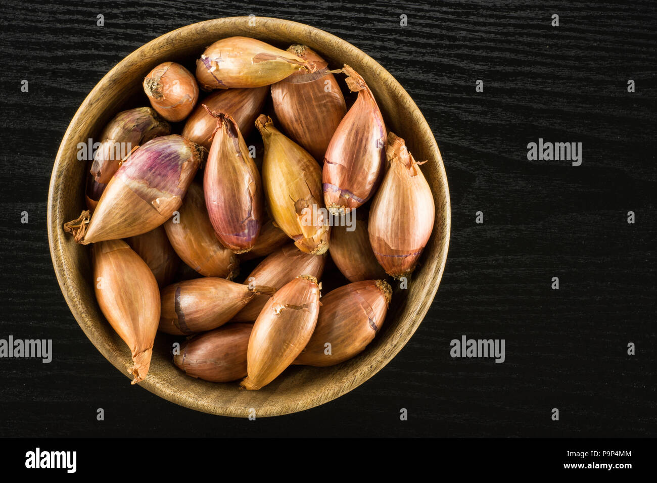 Long shallot in a wooden bowl top view isolated on black wood ...