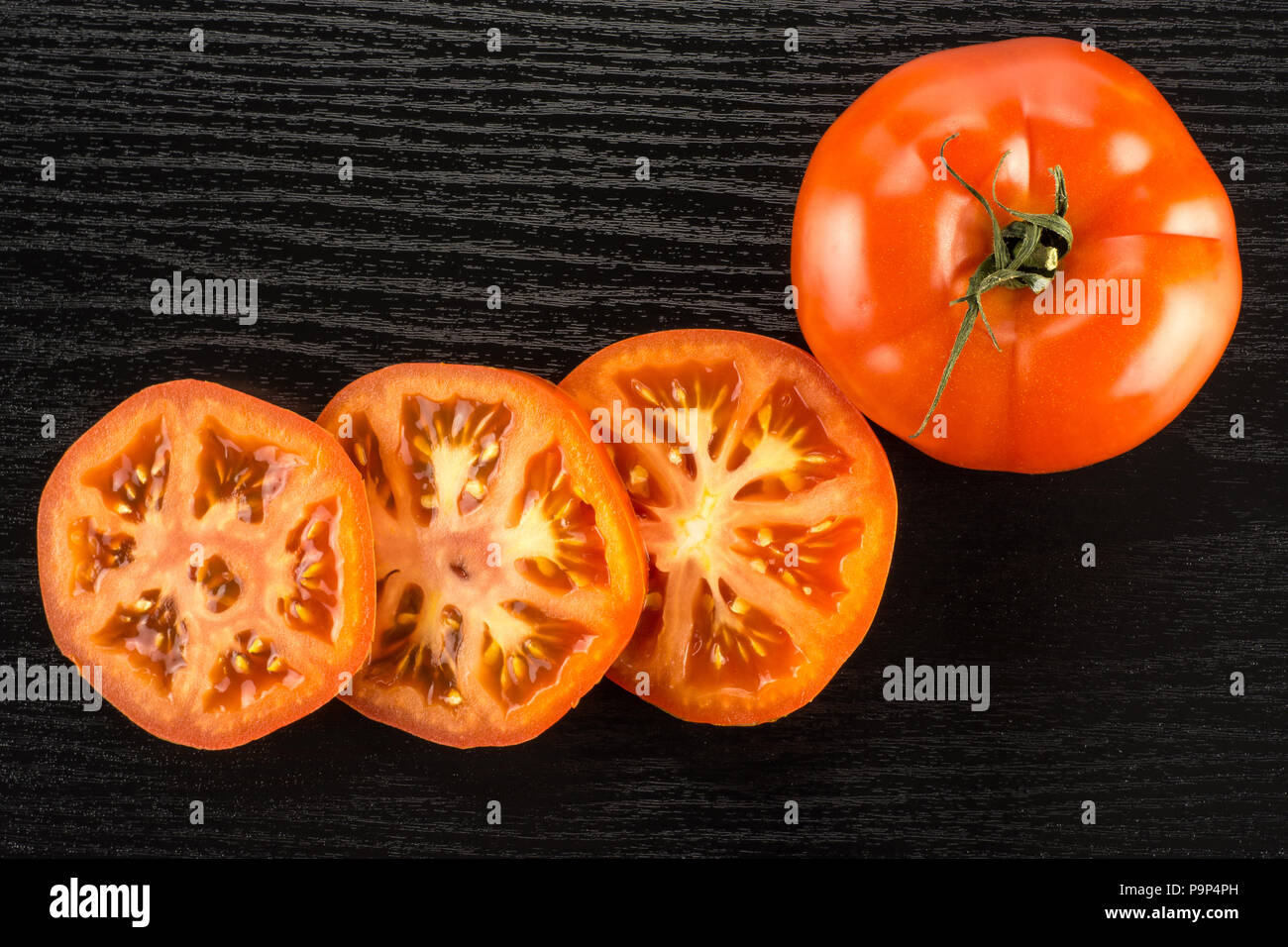One red tomato and three slices top view isolated on black wood ...