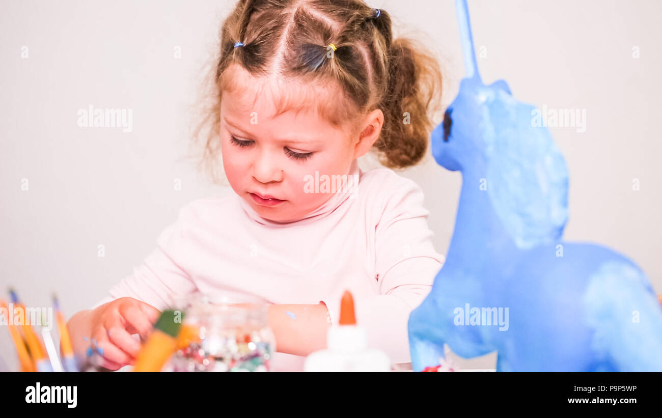 Little girl painting paper mache unicorn with blue paint Stock Photo ...