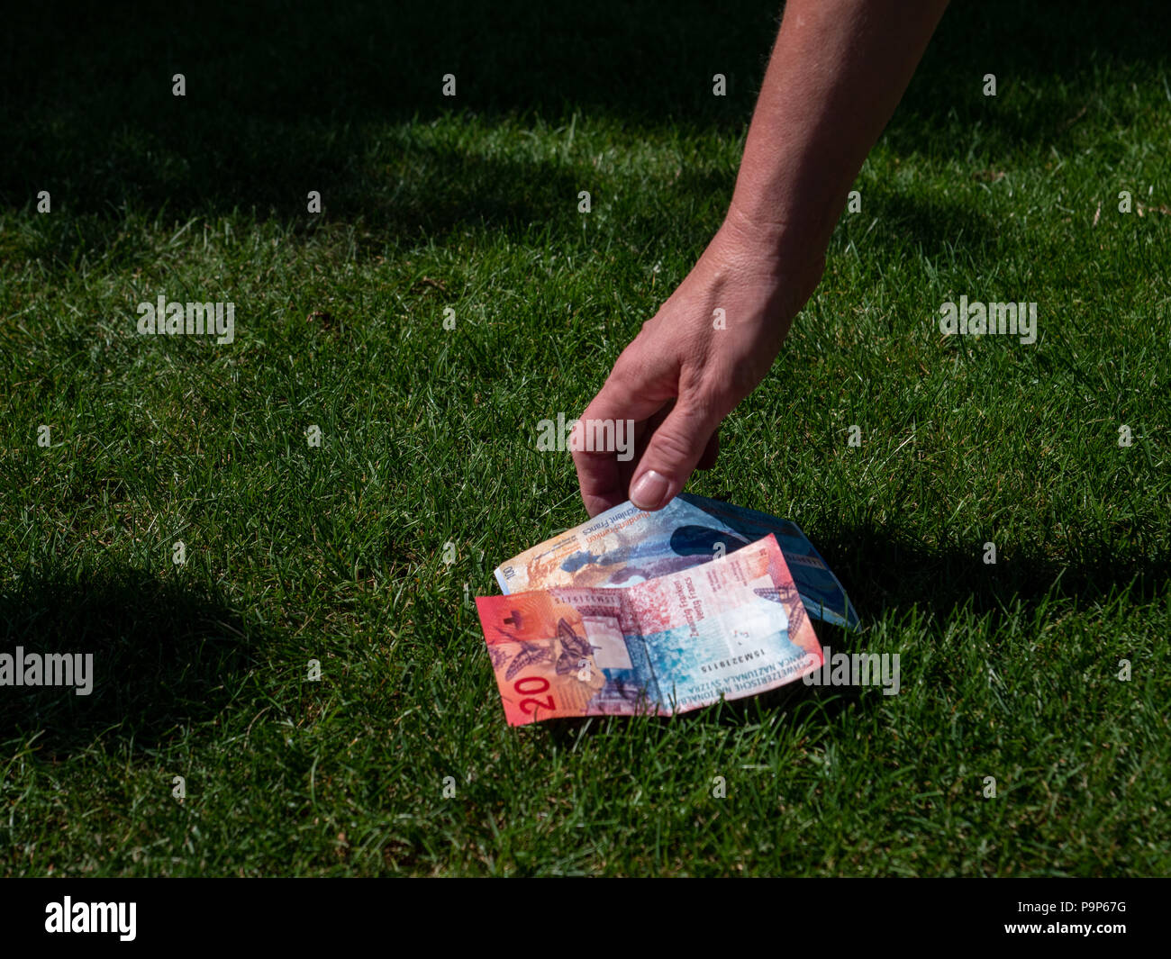 hand picking up money from the ground. swiss currency. grass ground ...