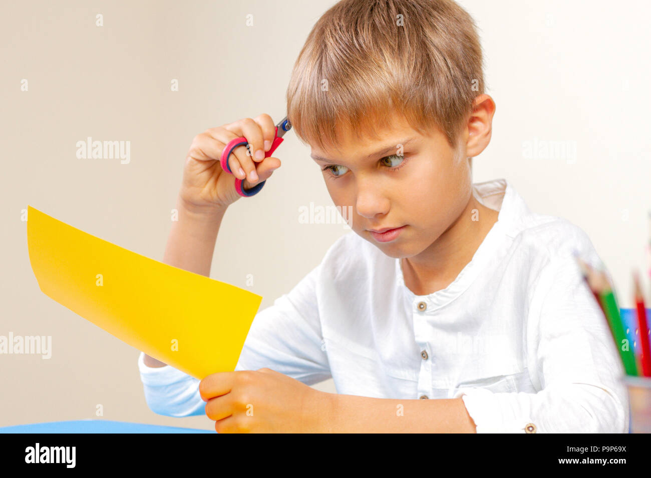 Child cutting colored paper with scissors at the table Stock Photo - Alamy