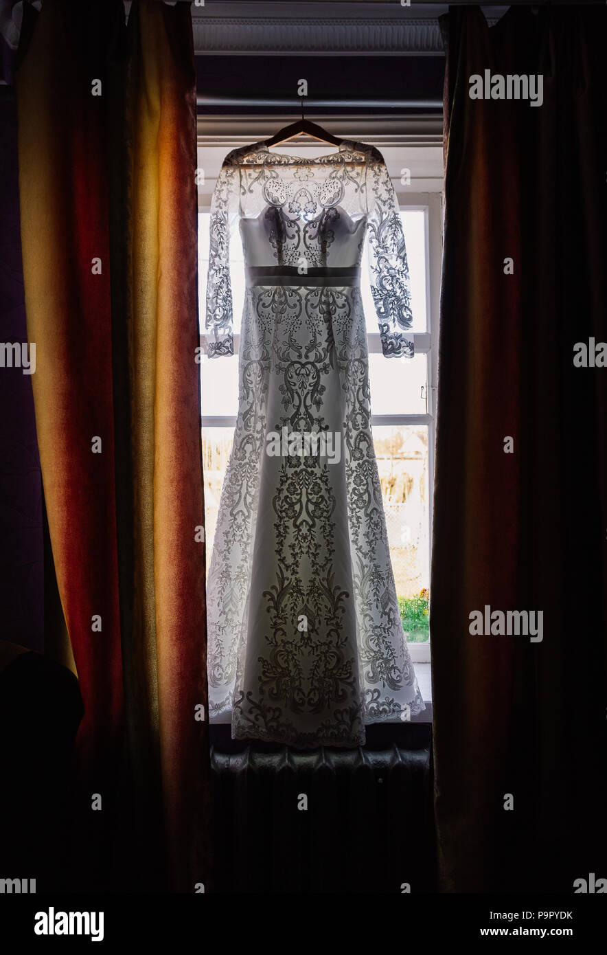Wedding dress hanging on the window in the room Stock Photo - Alamy