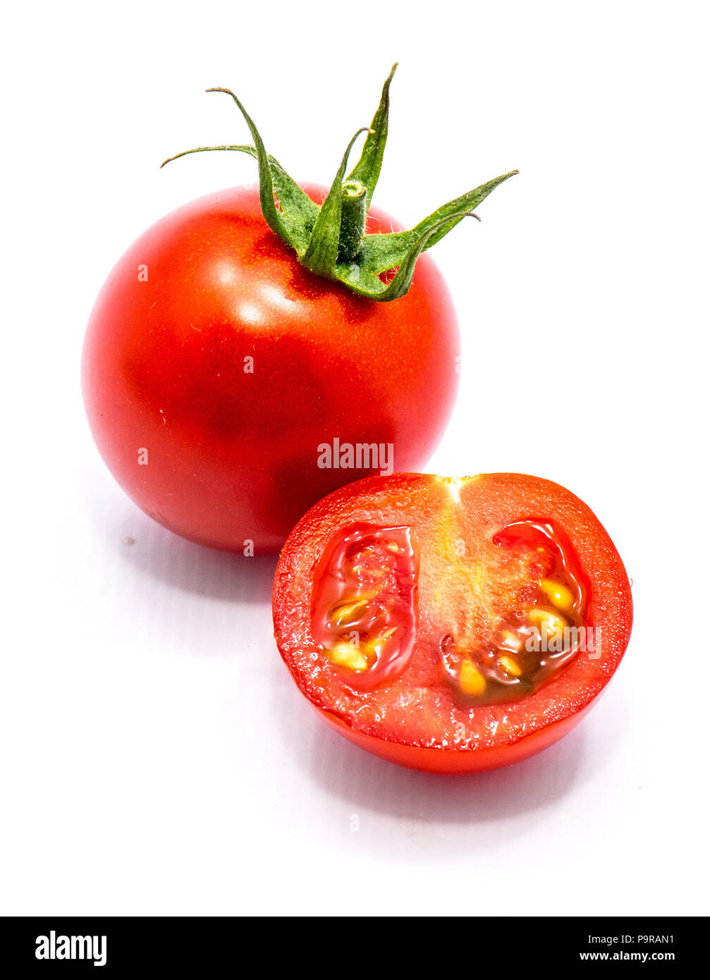 One whole red cherry tomato with green top and one half with seeds ...