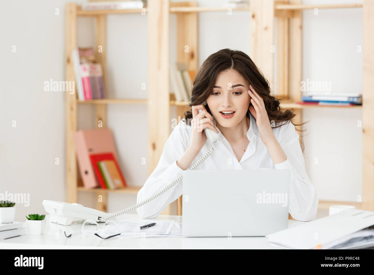 Portrait of smiling pretty young business woman sitting on workplace ...