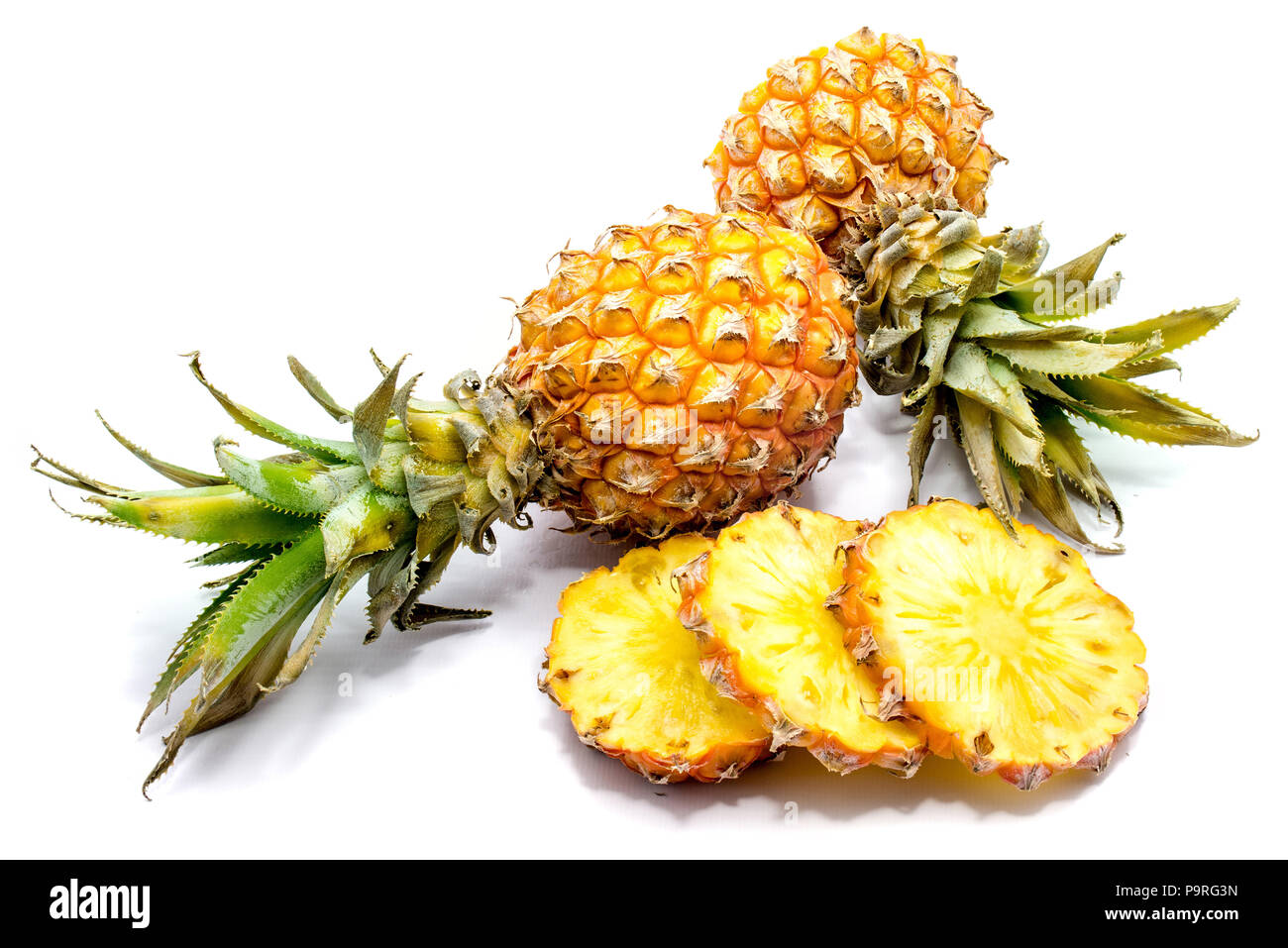 Fresh round pineapple slices and one whole pineapple with green leaves ...
