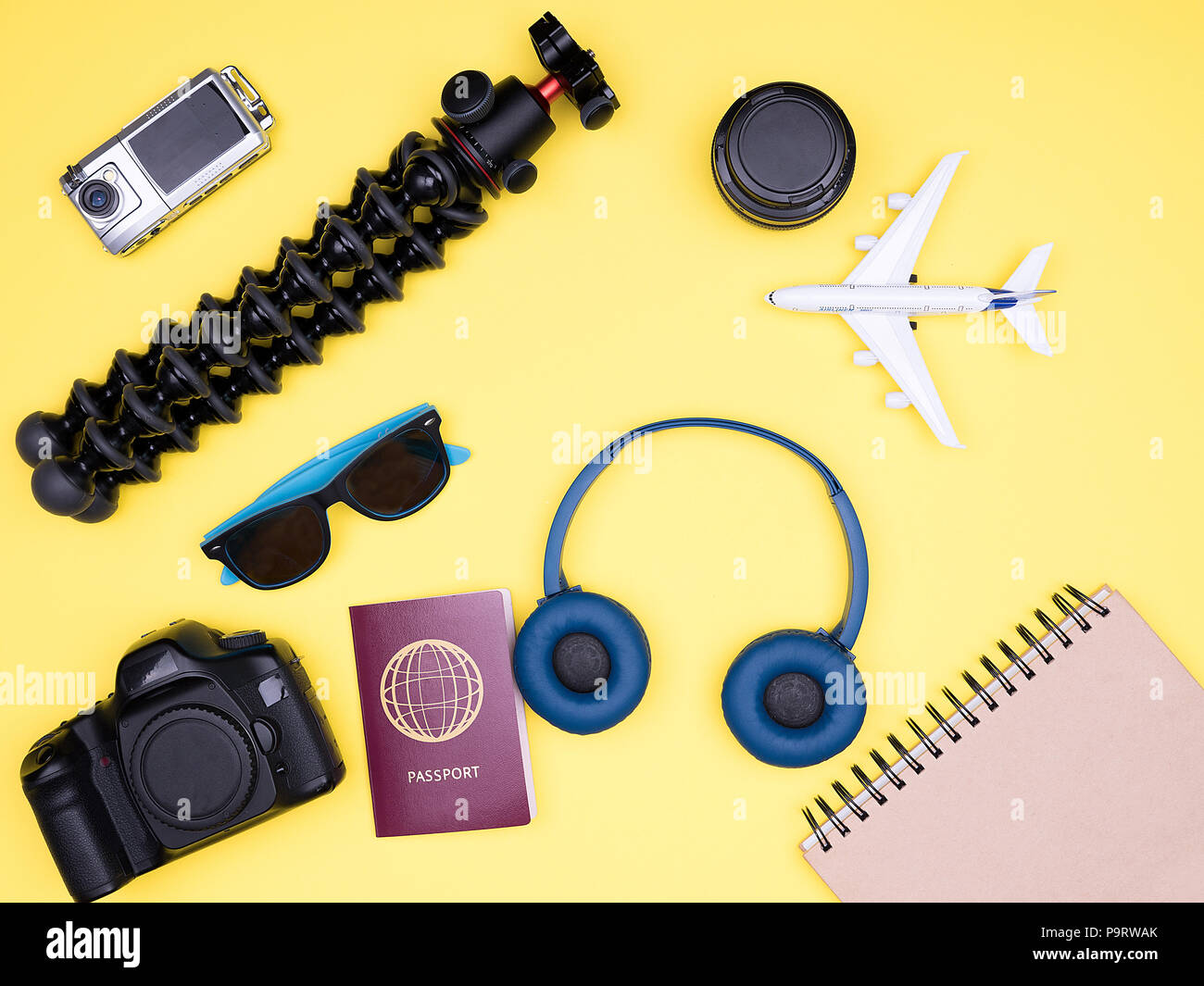 Top view of plane, camera, passport and sunglasses on yellow background ...