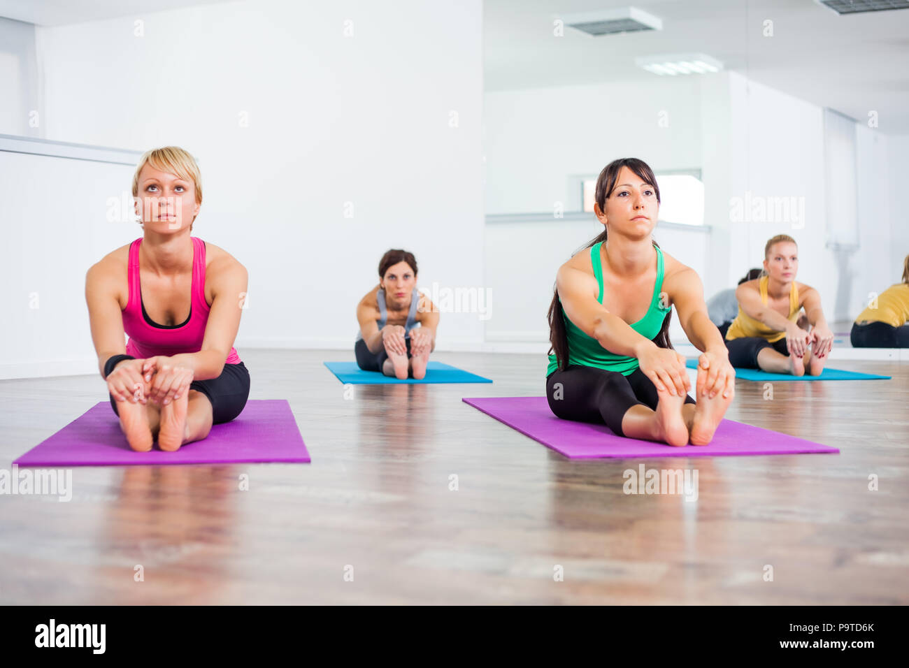 Four girls practicing yoga, Pascimottanasana / Seated Forward Bend pose ...