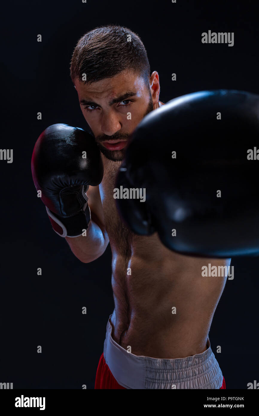 Portrait of tough male boxer posing in boxing stance against black ...