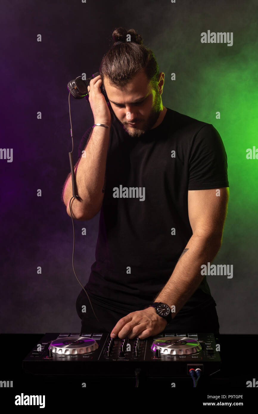 DJ playing music at mixer on colorful foggy background. A fashionable ...