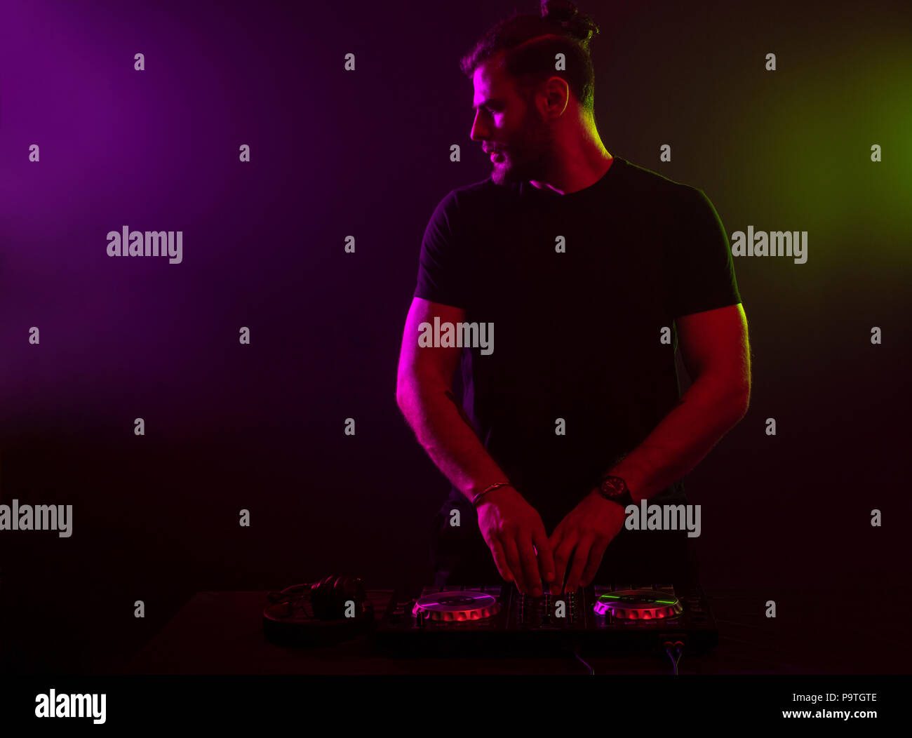 Handsome DJ in a black T-shirt at work mixing sound on her decks at a ...