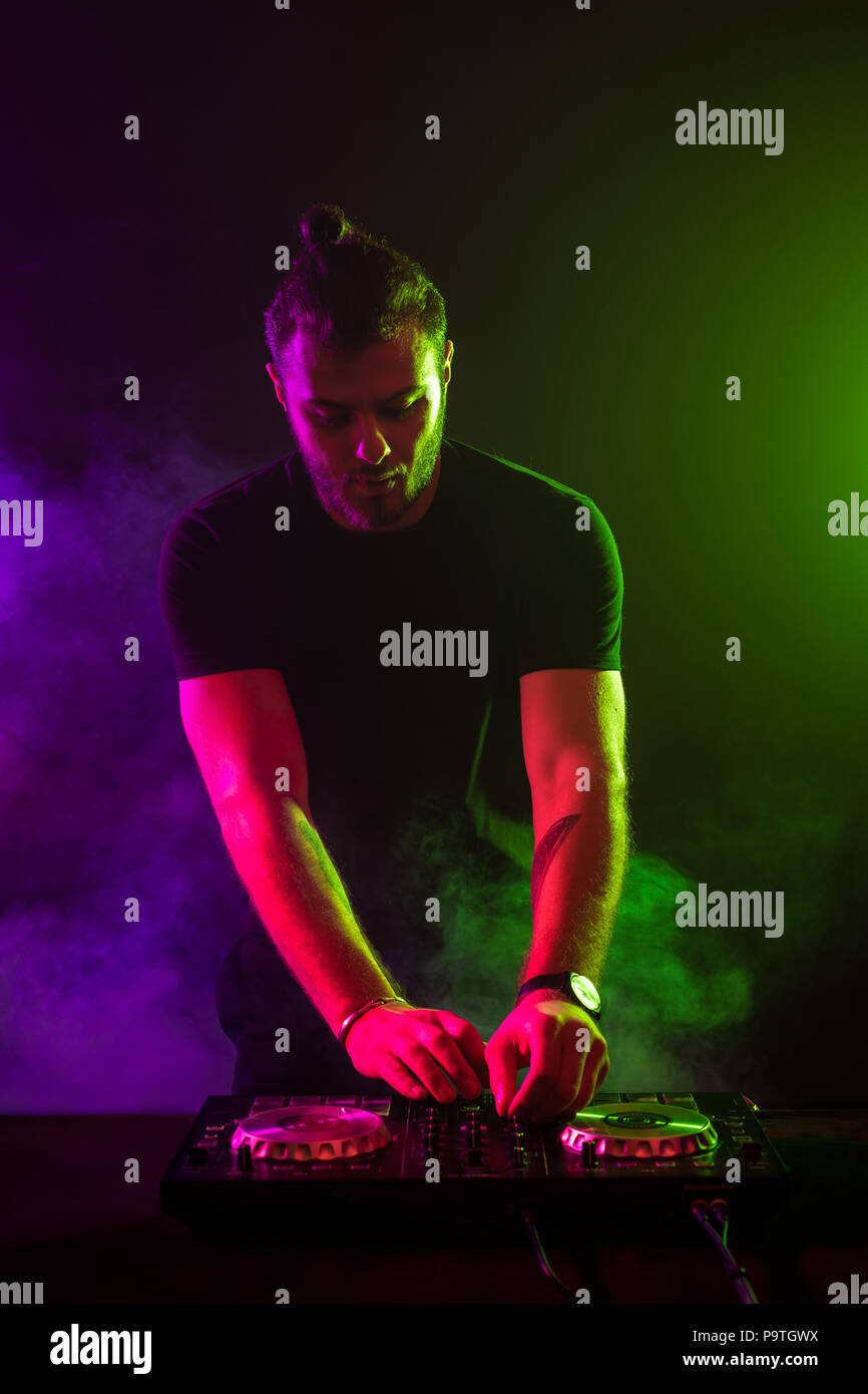 Attractive young DJ playing on turntables with color light effects. A ...