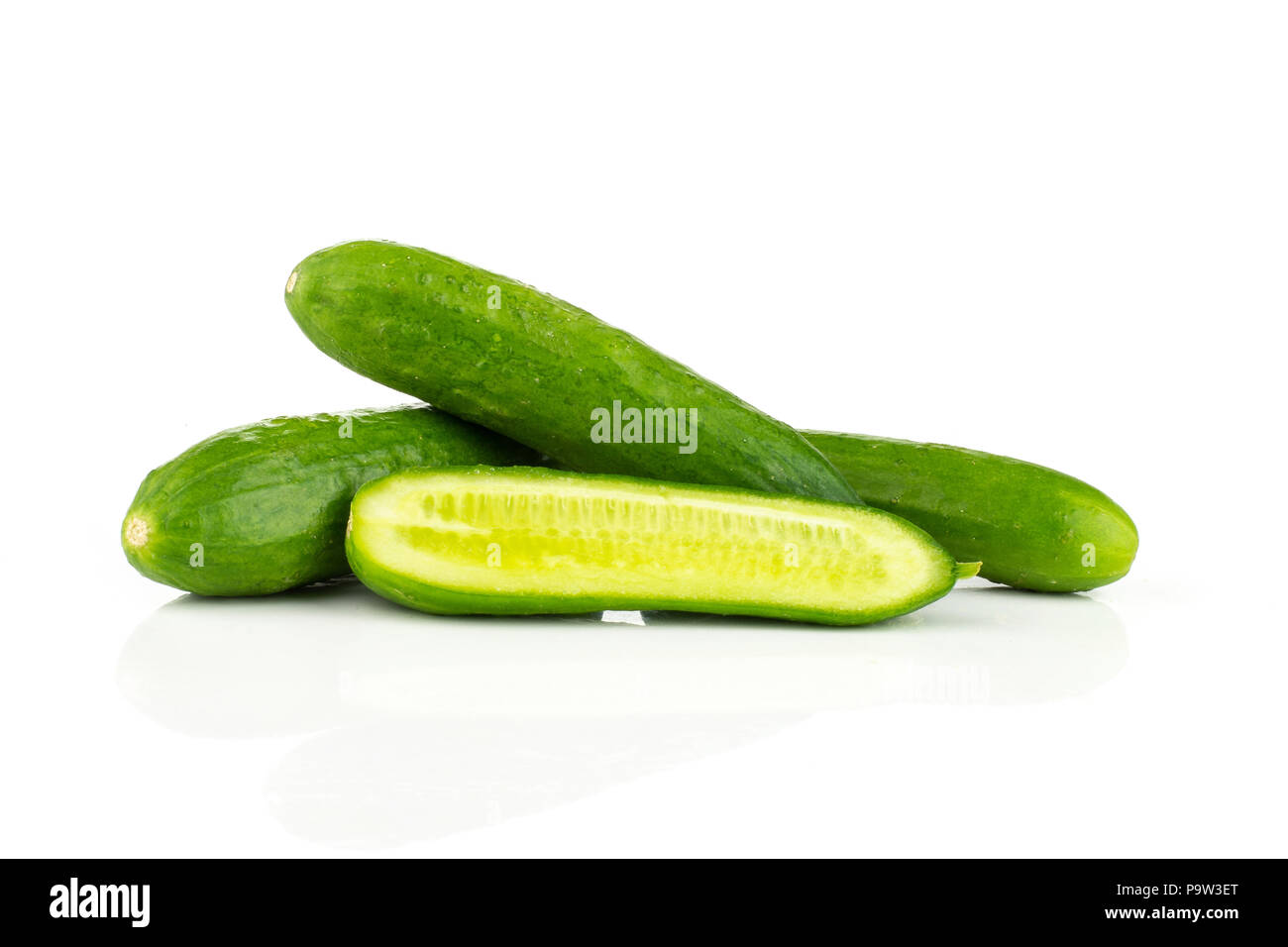 Three fresh green mini cucumbers and one section half isolated on white ...