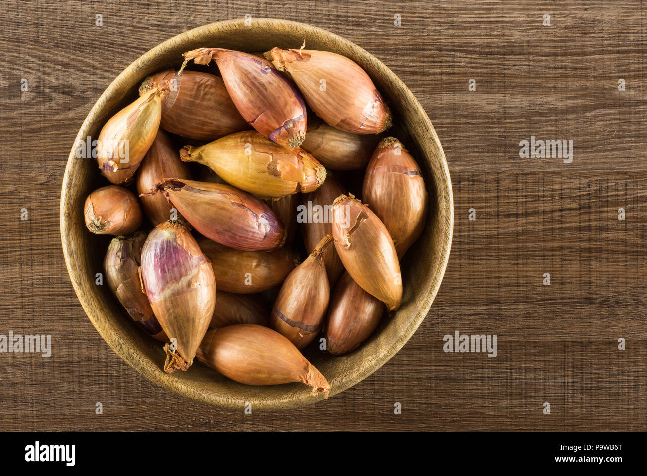 Long shallot in a wooden bowl top view isolated on brown wood ...