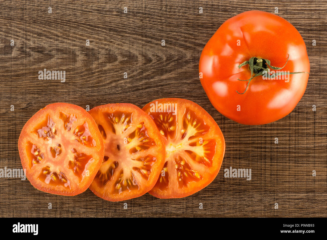 One red tomato and three slices top view isolated on brown wood ...