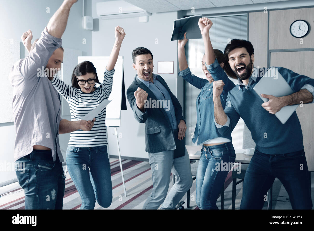 We did it. Overjoyed smiling young colleagues standing in the office ...