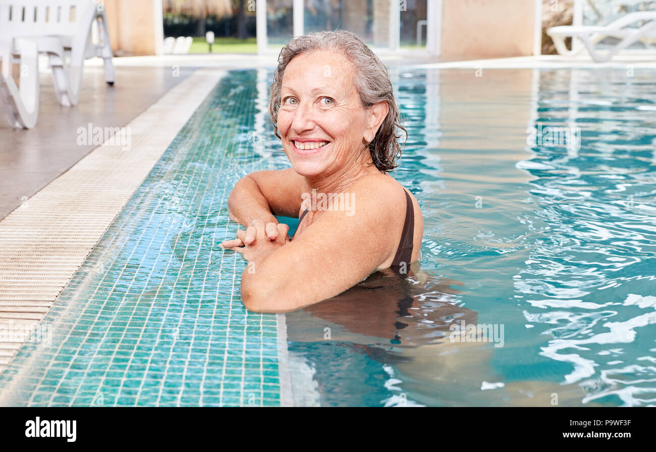 Vital senior woman at the poolside in a swimming pool or spa hotel ...