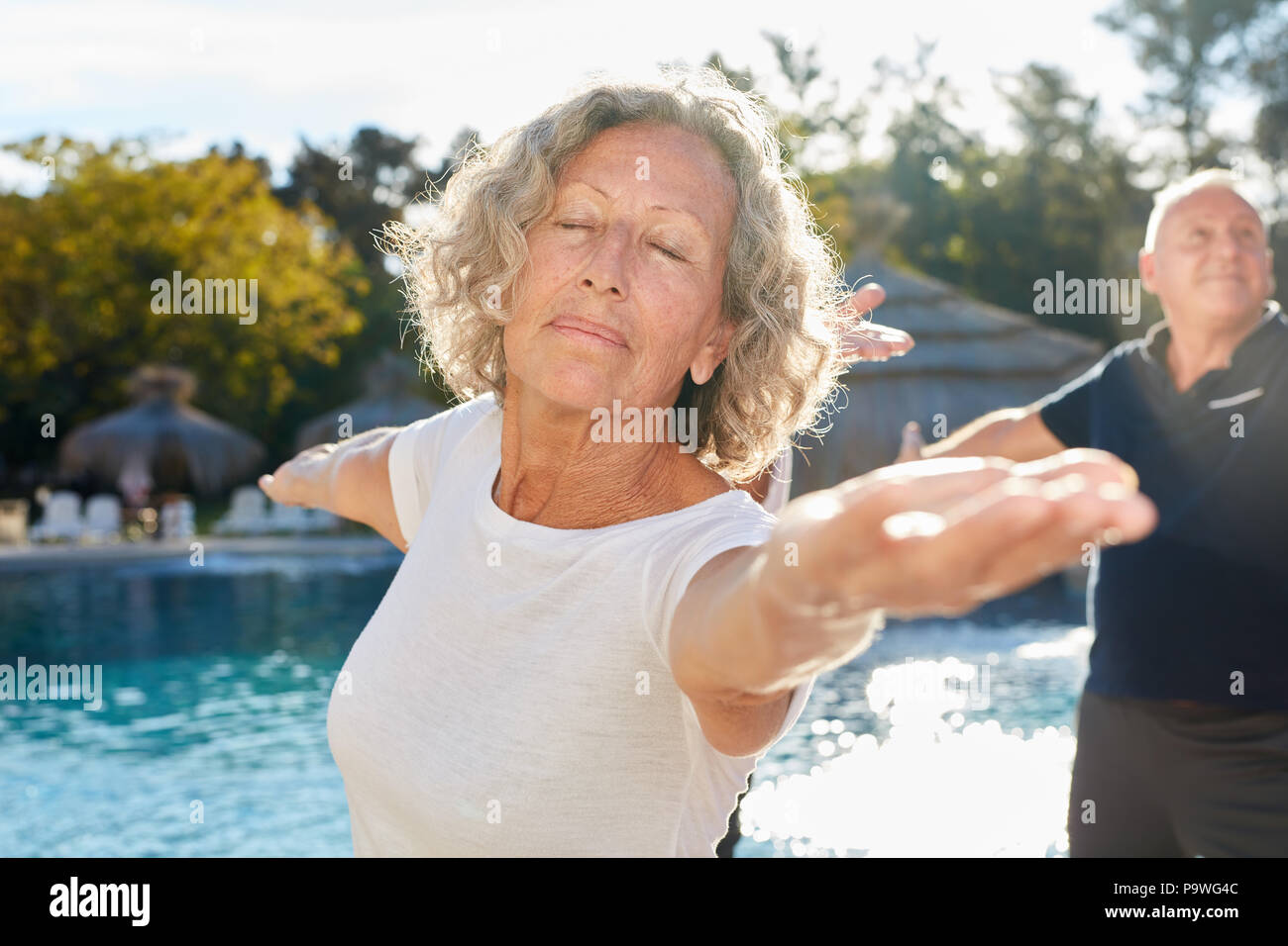 Old woman doing yoga exercise in workshop on spa vacation by the pool ...